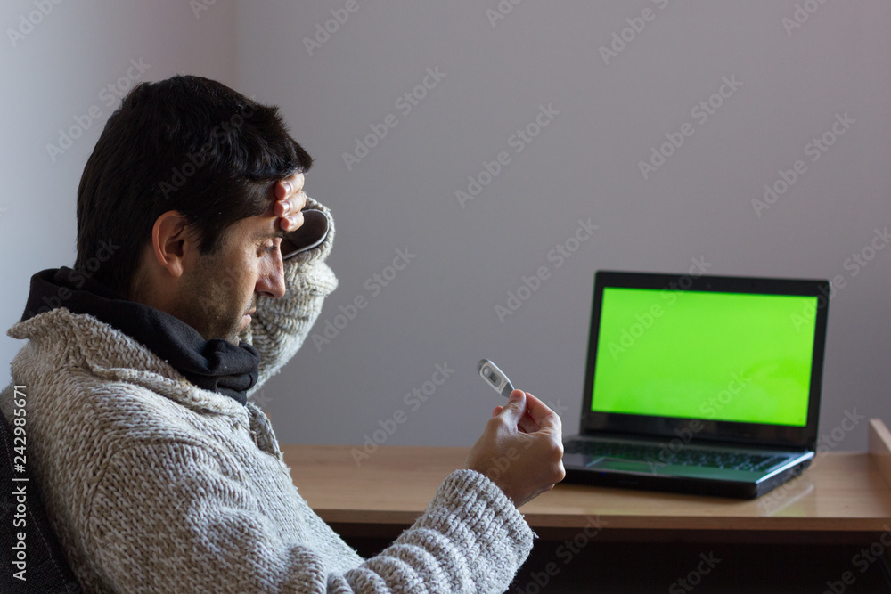 Man with fever looking at thermometer by computer chroma key in living ...