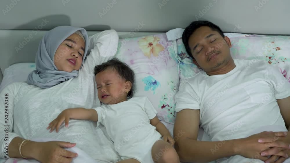 Little girl crying between her parents sleeping on the bed at home ...