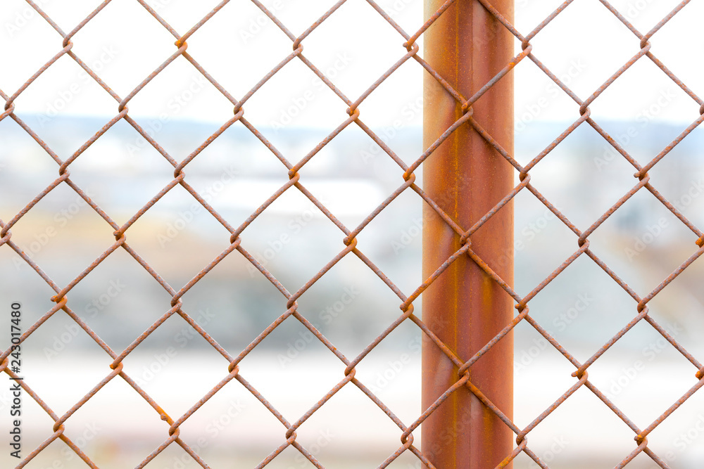 A closeup of a section of a rusty chain link fence. One fence post is ...