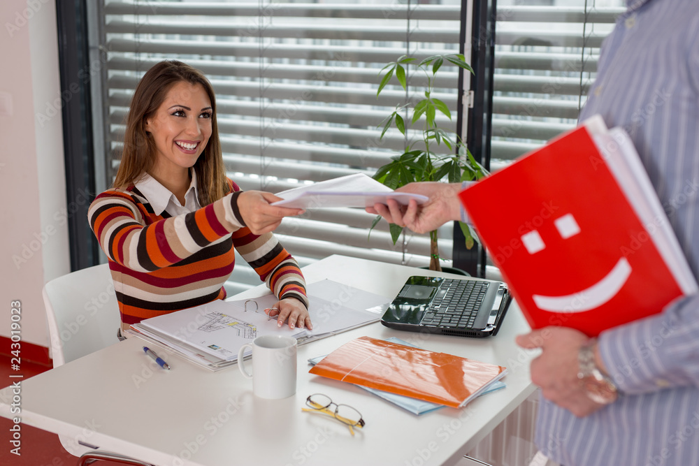 Beautiful young business woman handing over paperwork to her client at ...