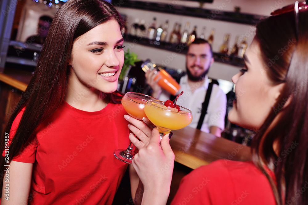 two young cute girls drink cocktails in a nightclub or bar, have fun ...