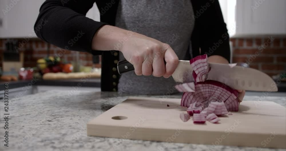 Woman dicing up a red onion in a bright kitchen. Young Millennial woman ...