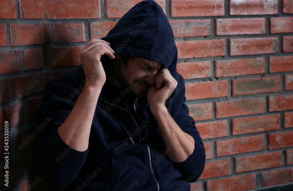 Young addicted man sitting near brick wall after using drugs Stock ...
