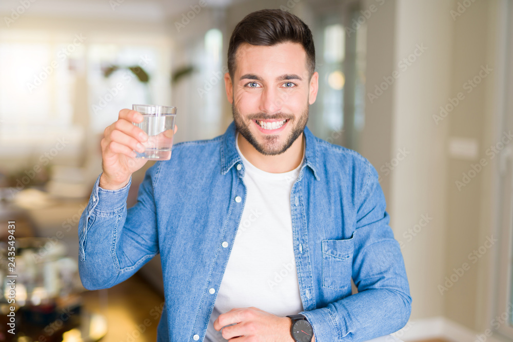 Young handsome man drinking a glass of water at home with a happy face ...