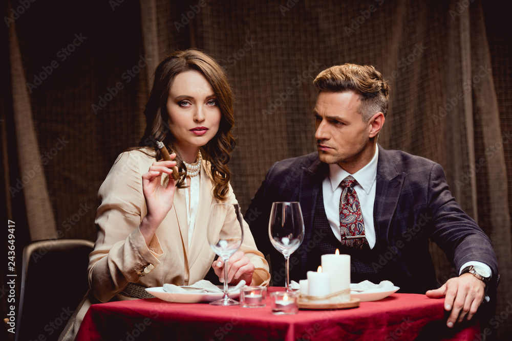 beautiful woman sitting at table and smoking cigar while having ...