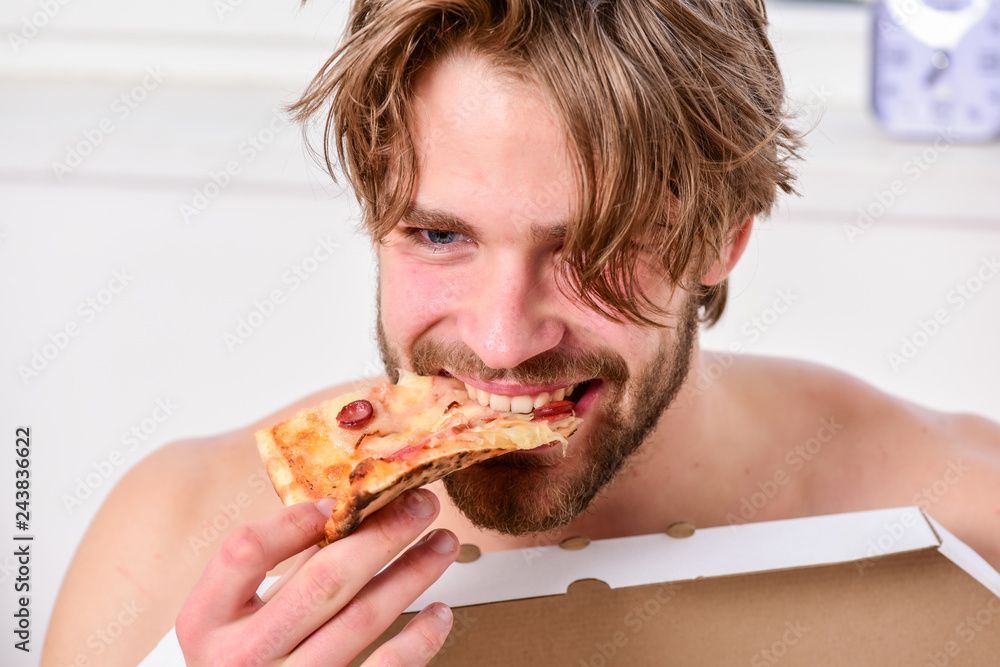 Guy holds pizza box sit bed in bedroom or hotel room. Hungry young man ...