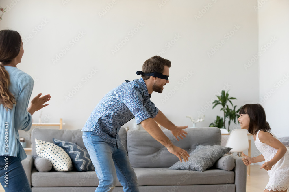 Blindfolded father playing hide and seek game with family at home, cute ...