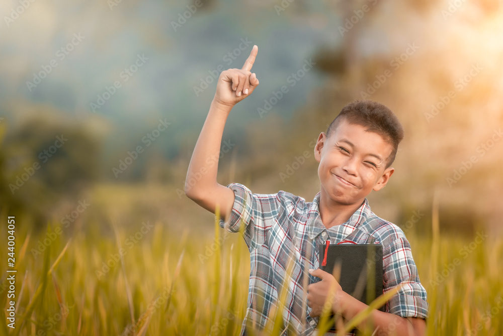 Happy boy standing and holding bible in rice field. young christian ...