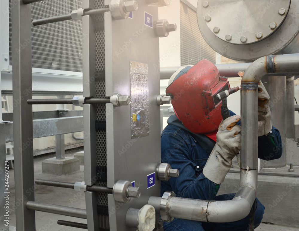 Welder arc welding metal piping of cooling water system in the factory ...