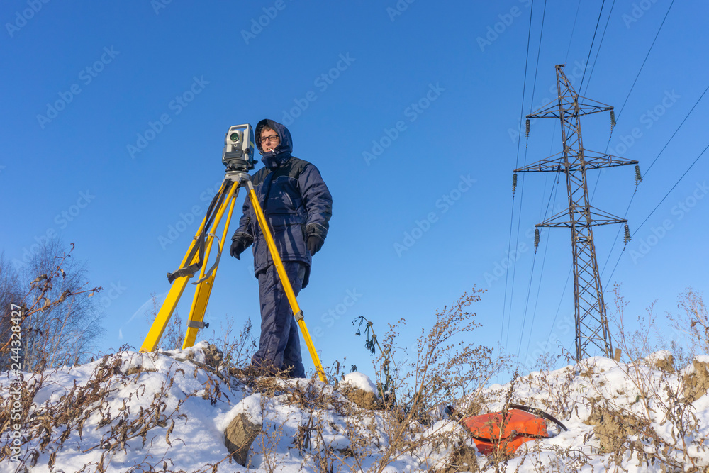 Surveyor in the winter on the construction site conducts topographic ...