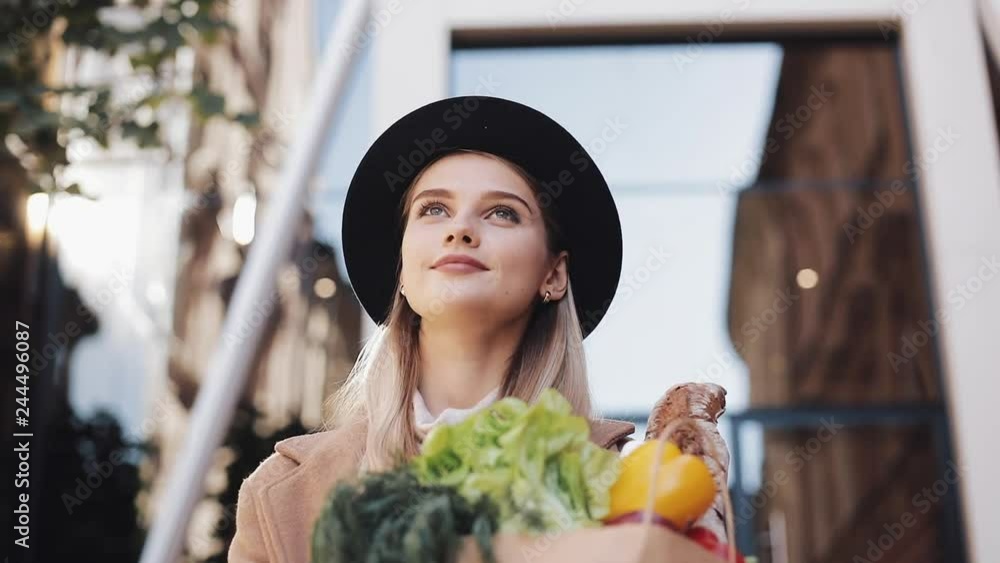 Young beautiful woman wearing stylish coat walking in the street holding a package of products ...