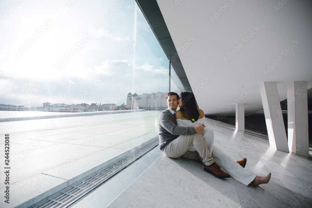 Beautiful asian couple sitting and hugging near big window in house ...