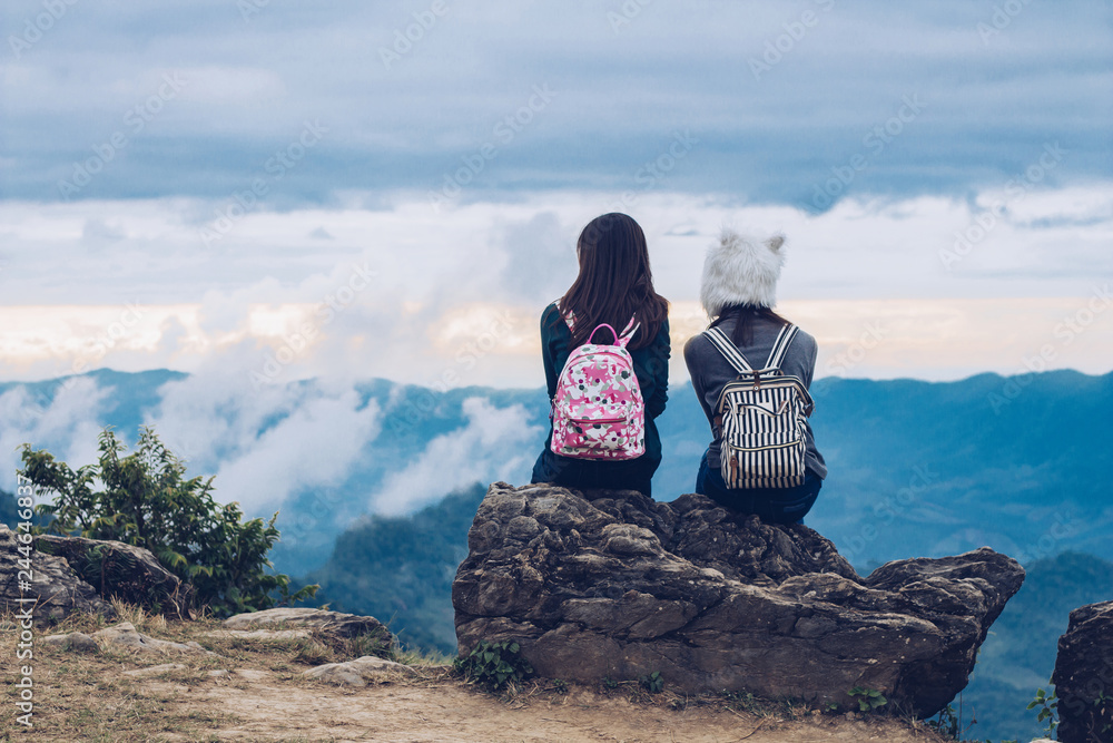 Two girls sit on a rock looking each other ,Blue sky with clouds and ...