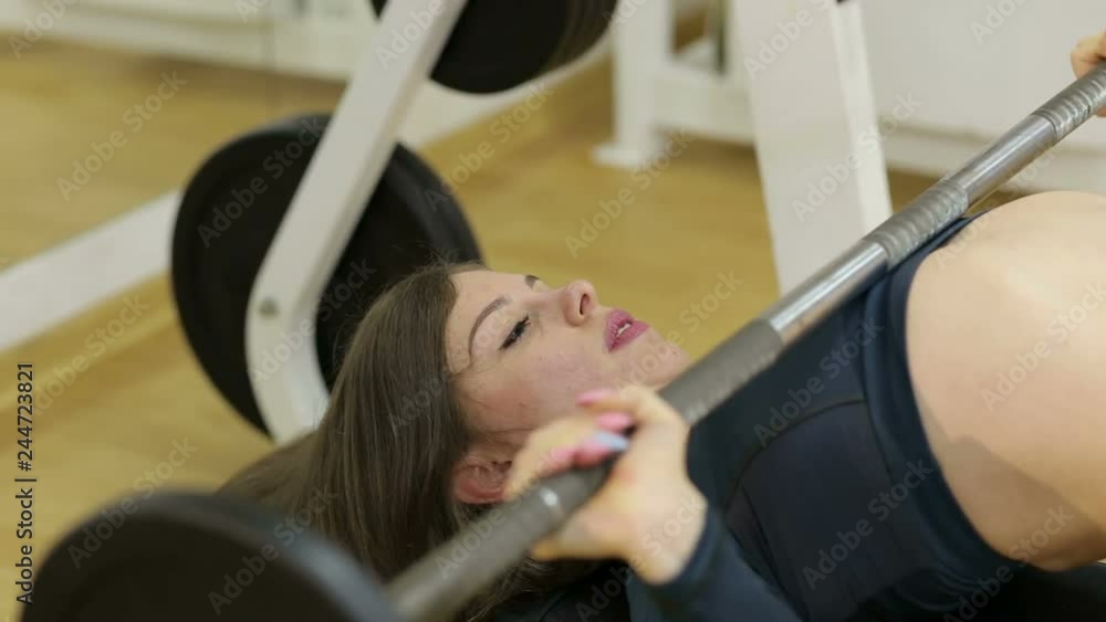Sporty girl doing an exercise with a bar in the supine position in the ...