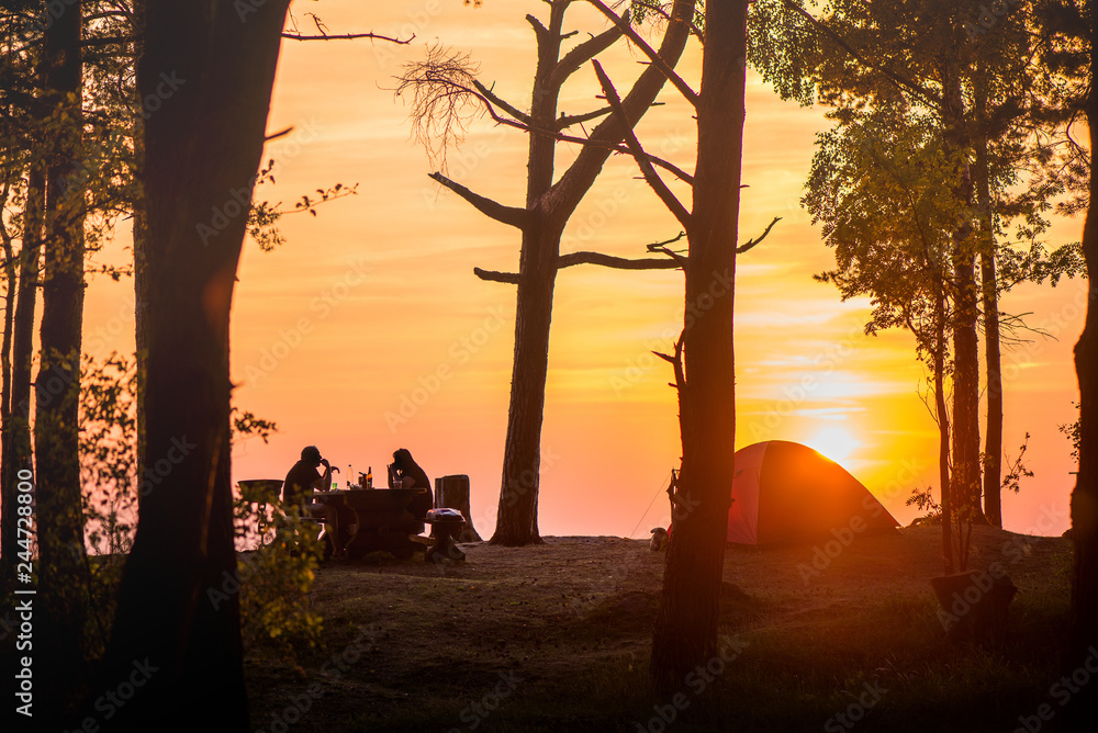 Camping on the beach during the sunset with silhouettes of young people ...