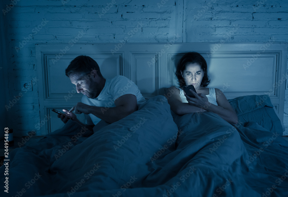Sad and bored couple addicted to smart mobile phones late at night in ...