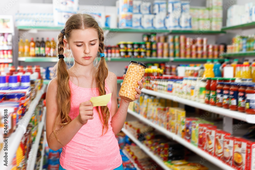 Positive tween girl choosing food products on shopping list in ...