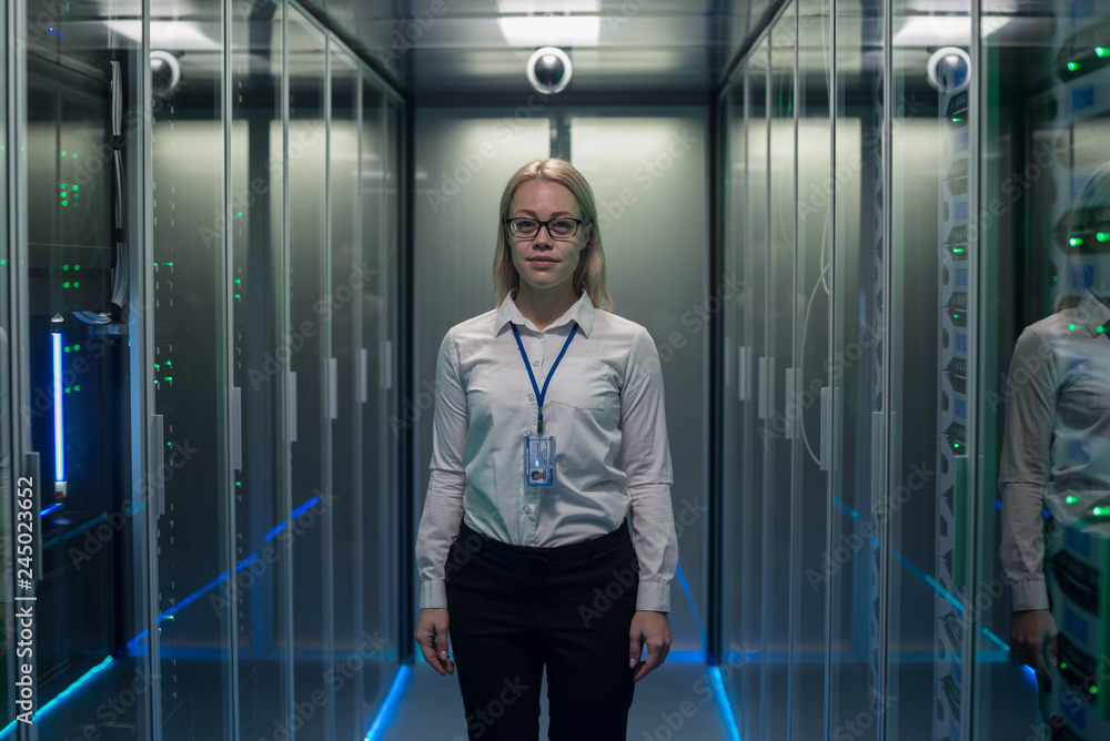 Adult IT worker in white shirt standing among server racks in data ...