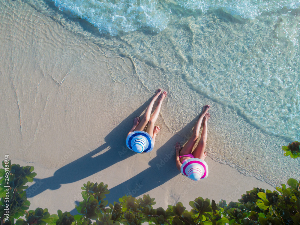aerial top view of 2 women wearing bikini with summer hat sitting on ...