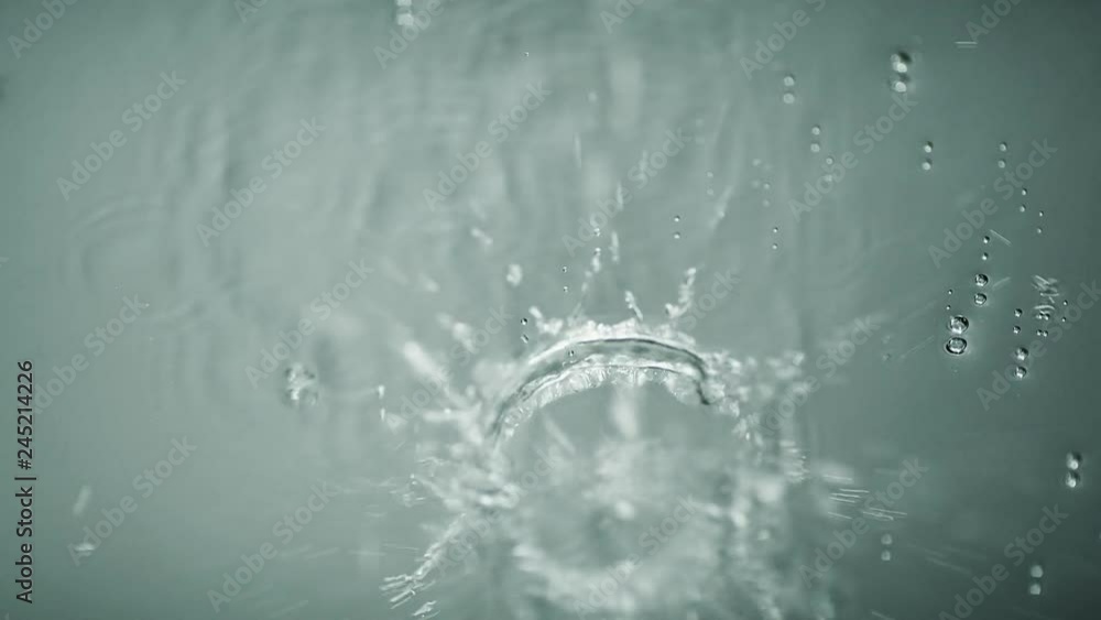 Water drops fall on a plain white mirrored surface. They splash in slow ...