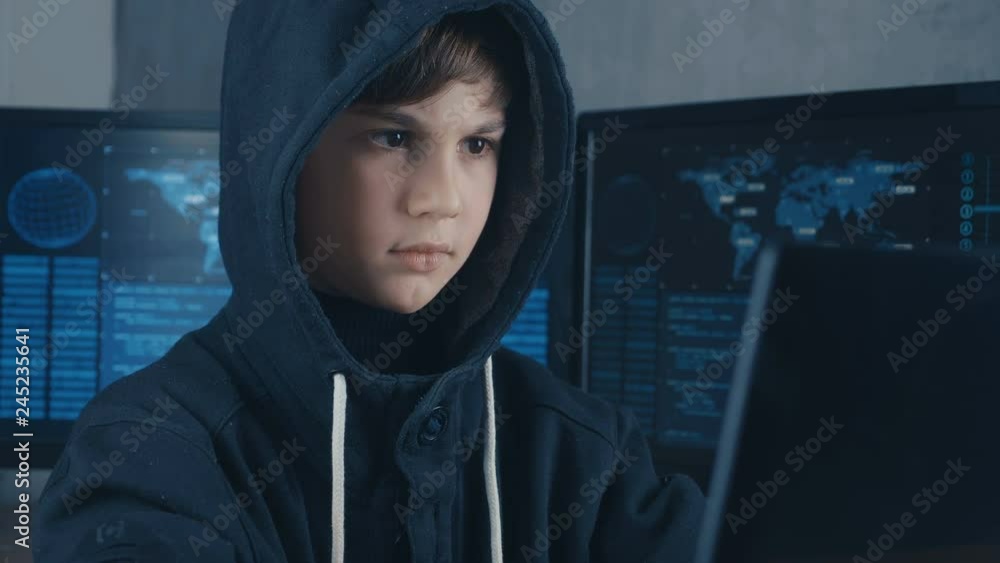 young prodigy boy hacker programmer in hood working at the computer in ...