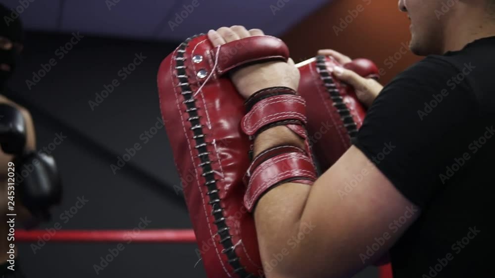 Male boxer and his coach work on the boxing paws in the ring practicing ...