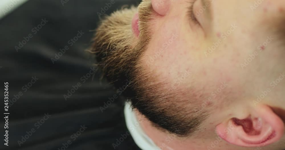 Handsome caucasian man getting a beard cut in a modern barber shop. 4K ...