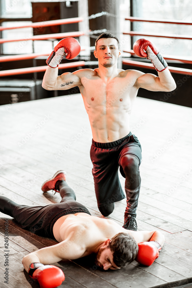 Beaten boxer lying knocked out on the boxing ring with strong man ...