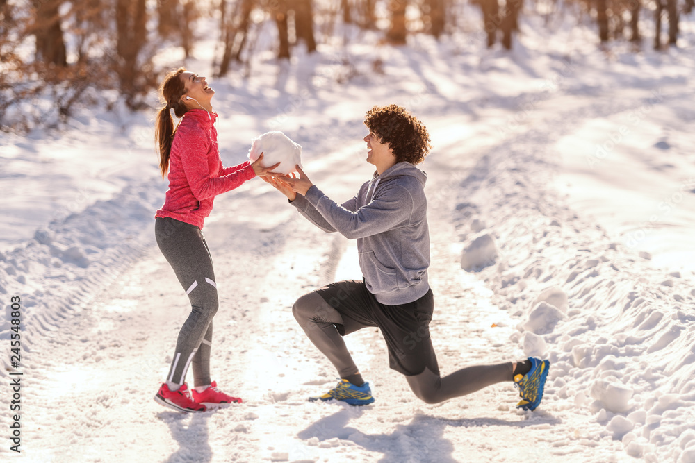 Runners on the snow. Man kneeling and giving to woman big snowball ...