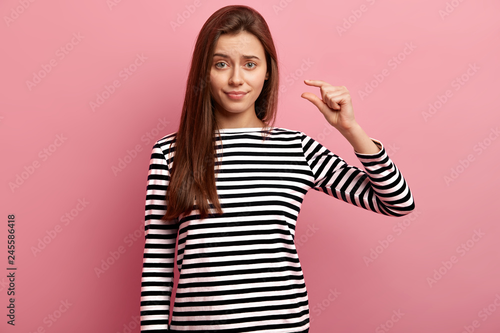 Indoor photo of pleasant looking young woman shows tiny thing with sad ...