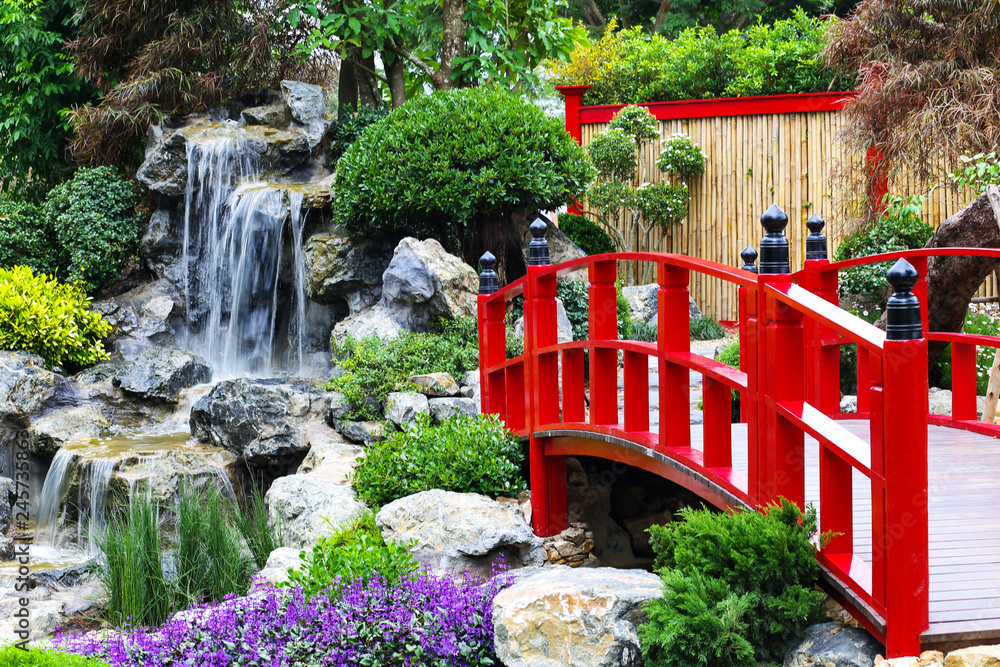 Red bridge and artificial waterfall cover with trees and colorful ...