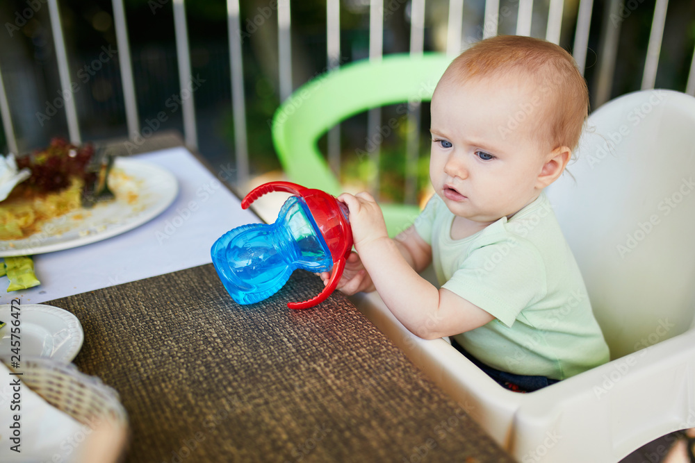 Little baby girl sitting in high chair and drinking water from sippy ...
