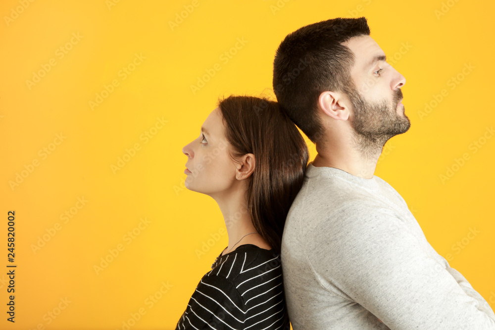 Side profile of a young couple standing back to back against yellow ...