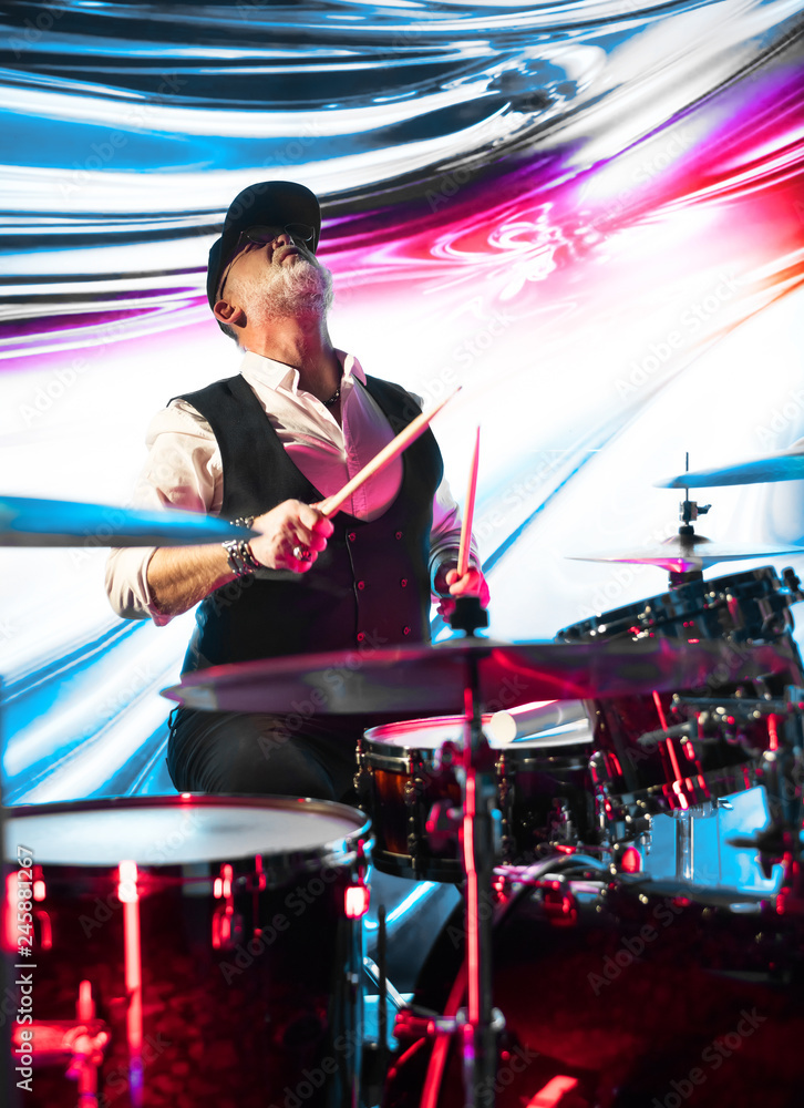 Professional drummer playing on drum set on stage in the color light ...