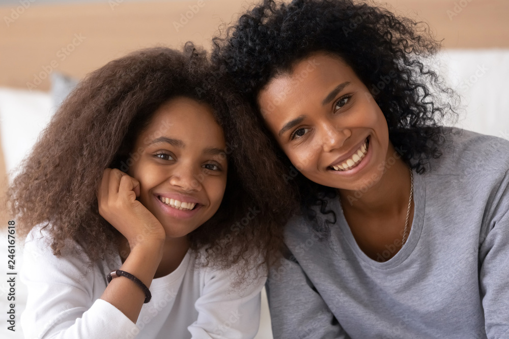 Portrait Of Smiling Black Mother And Daughter Lying On Bed Looking At