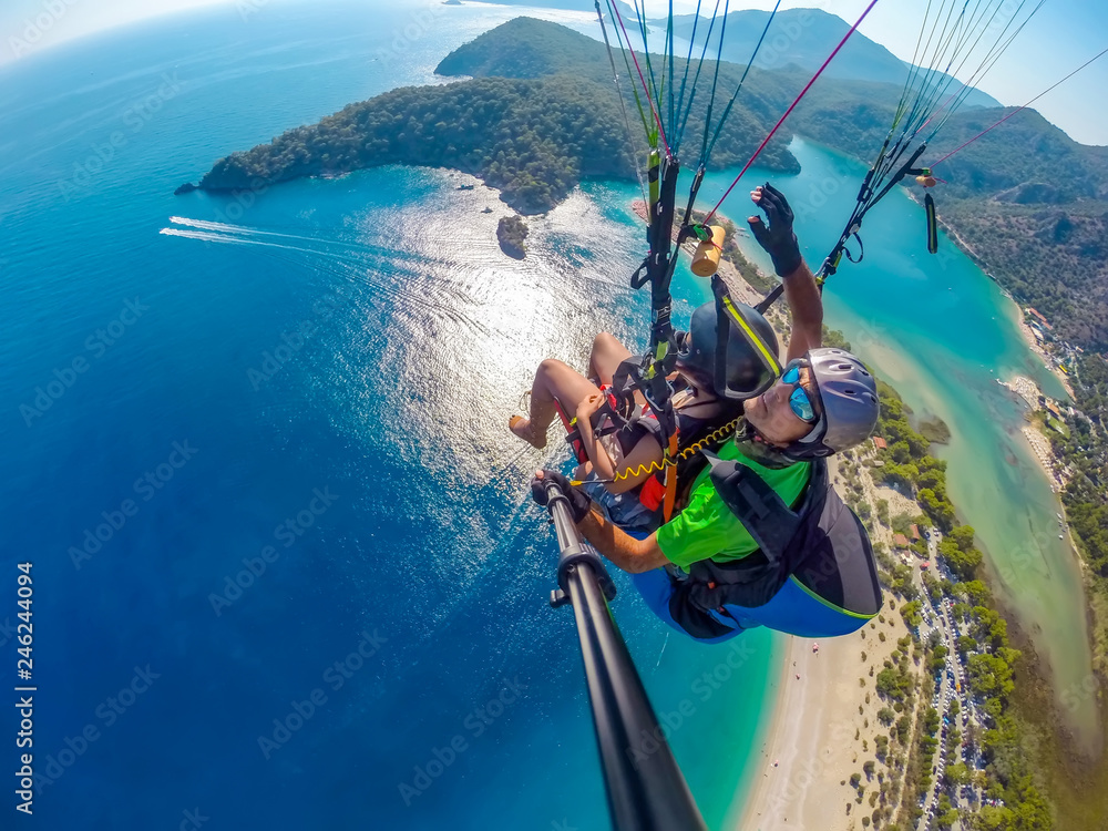 Paraglider tandem flying over the sea with blue water and mountains in ...