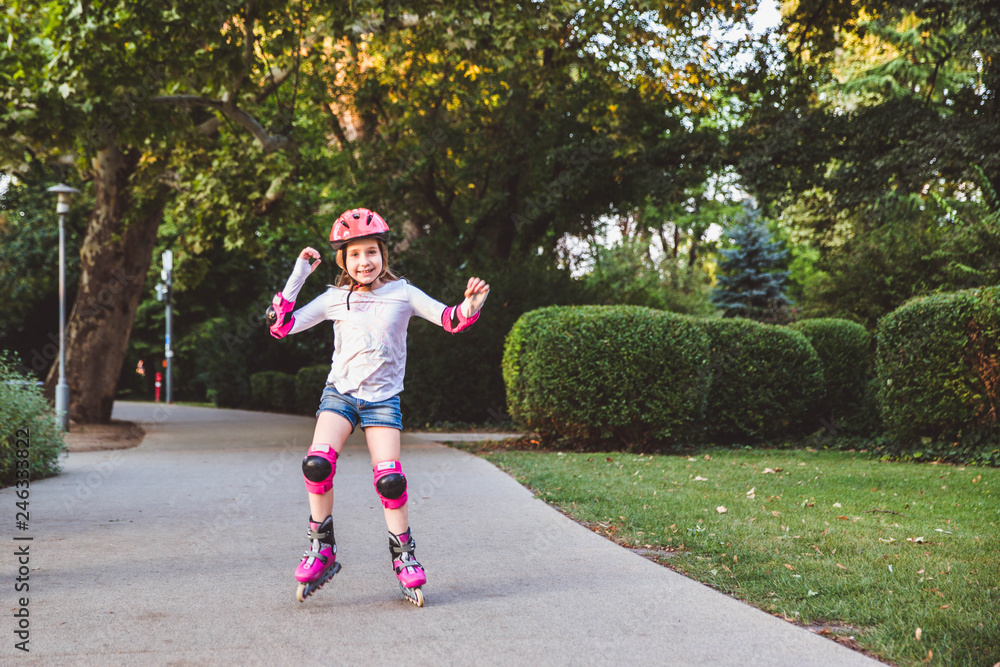 Little girl rides on rollers in summer park. Child wearing protection ...