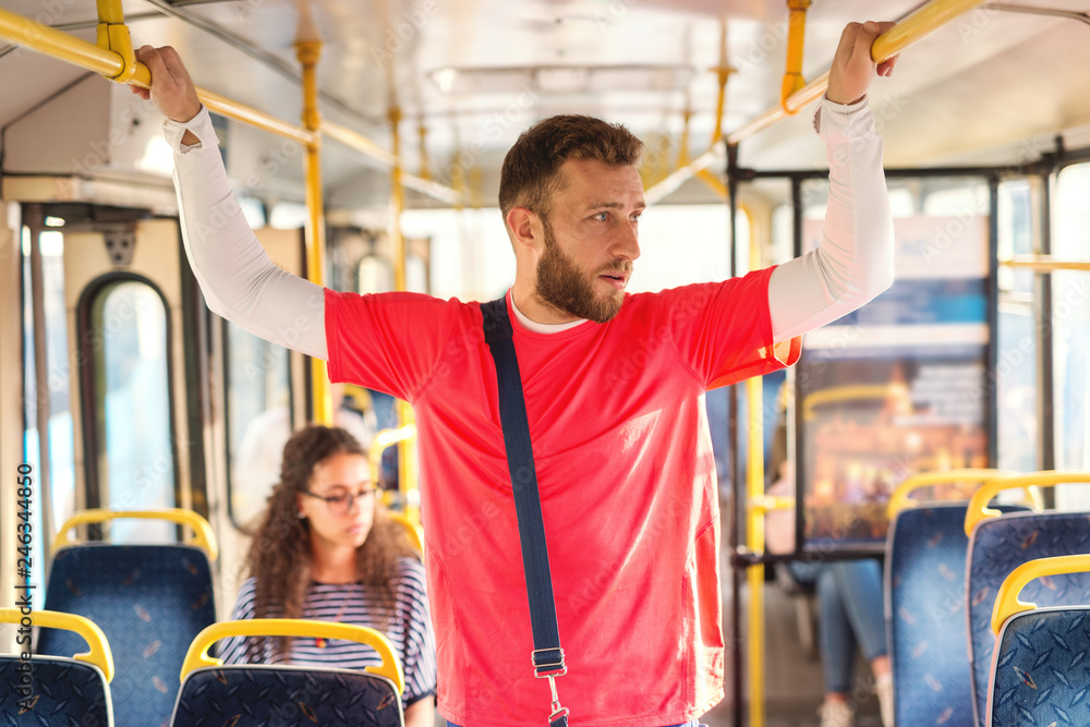 Young man standing in a bus, holding to hand-grip , looking trough ...