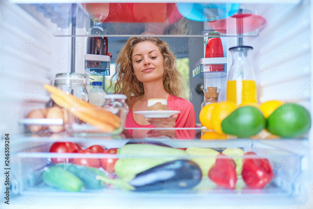 Woman taking gateau form fridge full of groceries. Unhealthy eating ...