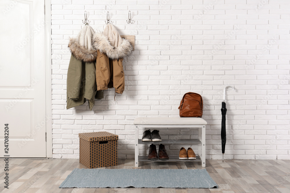 Stylish hallway interior with shoe rack and hanging clothes on brick ...