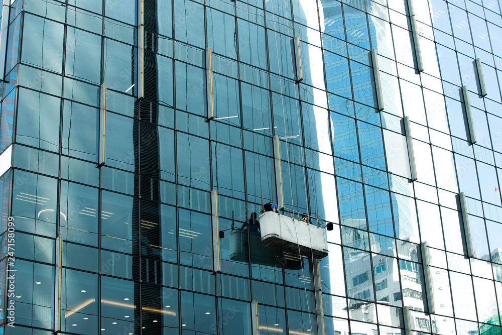 Workers crane cradle clean windows glass of high building under sun day ...