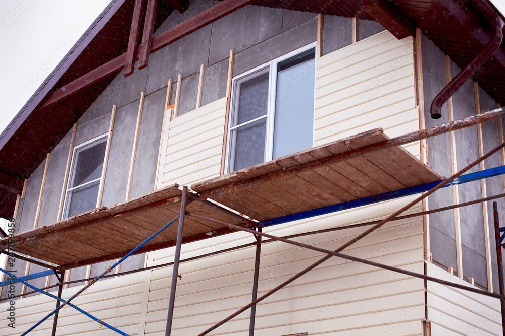 Scaffolding around house with beige siding covering walls. Construction ...