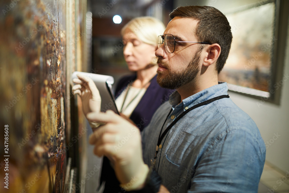 Waist up portrait of two museum workers inspecting painting for ...