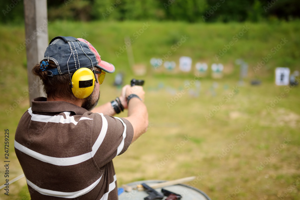 Man shooting on an outdoor shooting range. Male aiming gun at firing ...