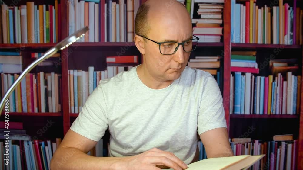 Attractive thoughtful man read book at table late evening. Turn off ...