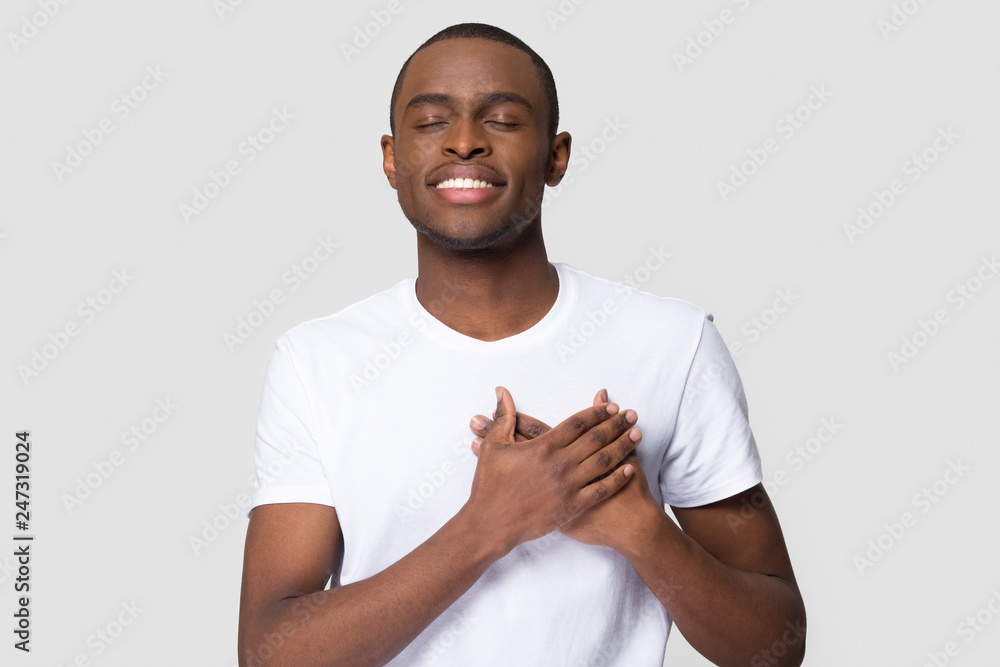 Grateful happy pleased african man holding hands on chest to heart ...