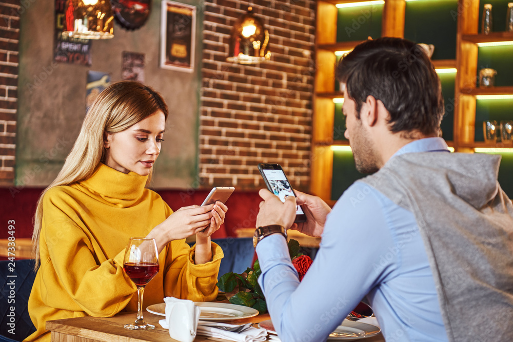 Always with smartphone. Young couple are sitting in restaurant with ...