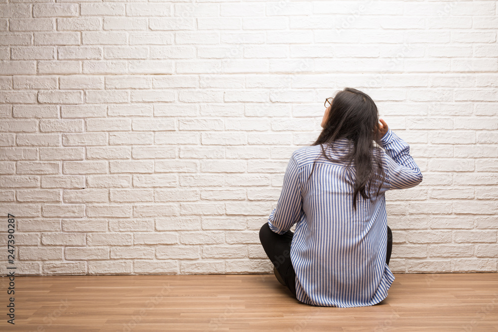 Young indian woman sit against a brick wall showing back, posing and ...