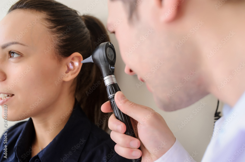 lateral view of a male otolaryngologist examining the ear of a female ...