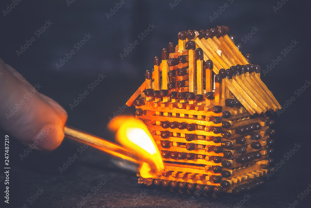 Foto de hand with a burning match sets fire to the house model of ...